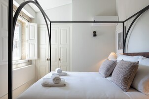 Cama bem arrumada com toalhas enroladas, cabeceira e ar-condicionado fixado na parede.