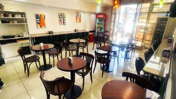 Um café com várias mesas e cadeiras, um refrigerador de Coca-Cola e obras de arte nas paredes.
