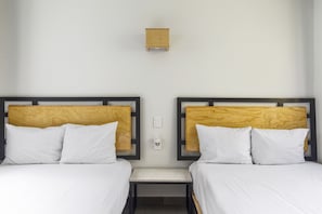 Quarto de hotel com duas camas, cada uma com roupa de cama branca e cabeceiras de madeira.