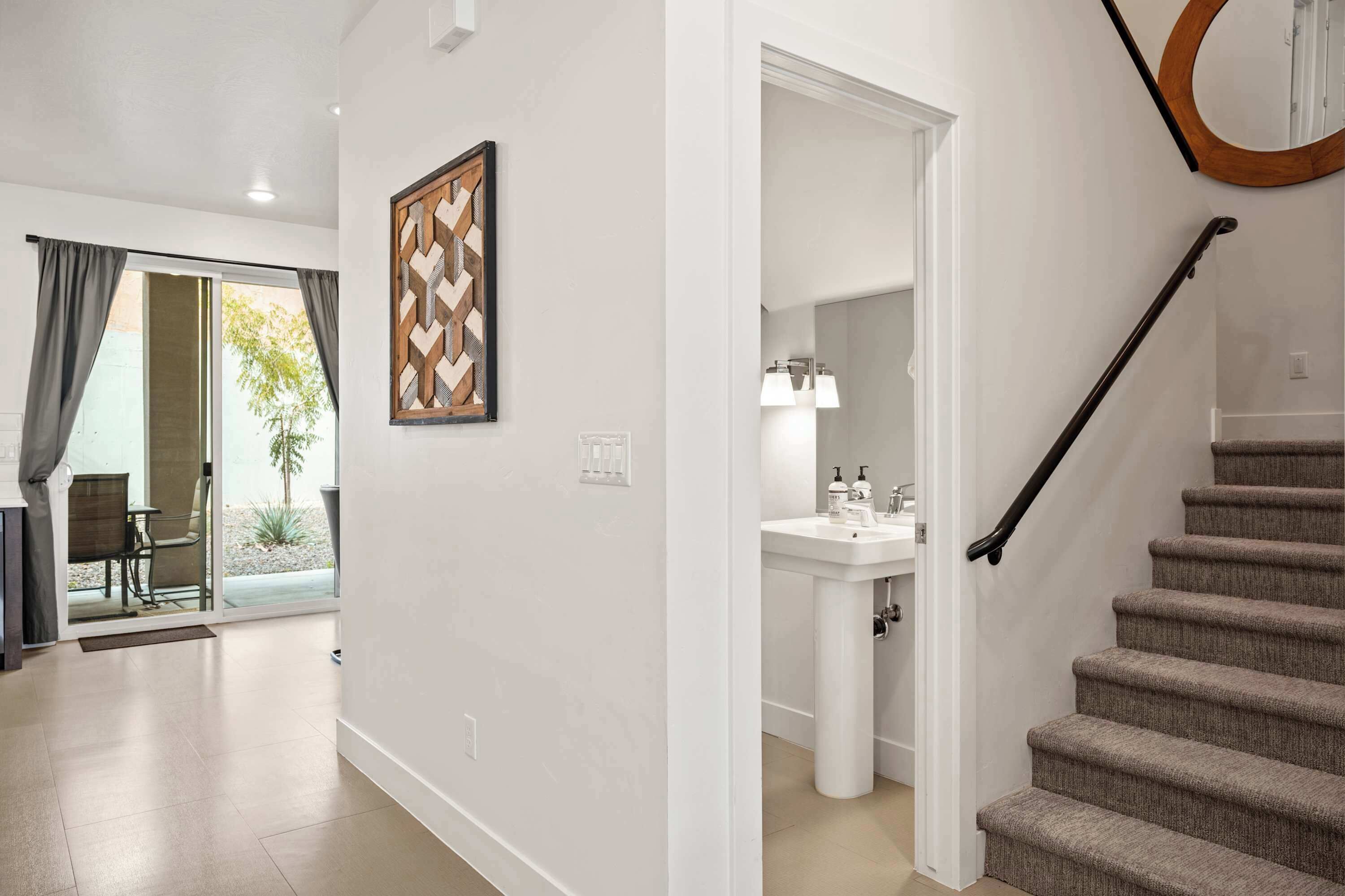Um interior moderno com escada, banheiro com pia e espelho, e área de jantar com mesa e cadeiras.