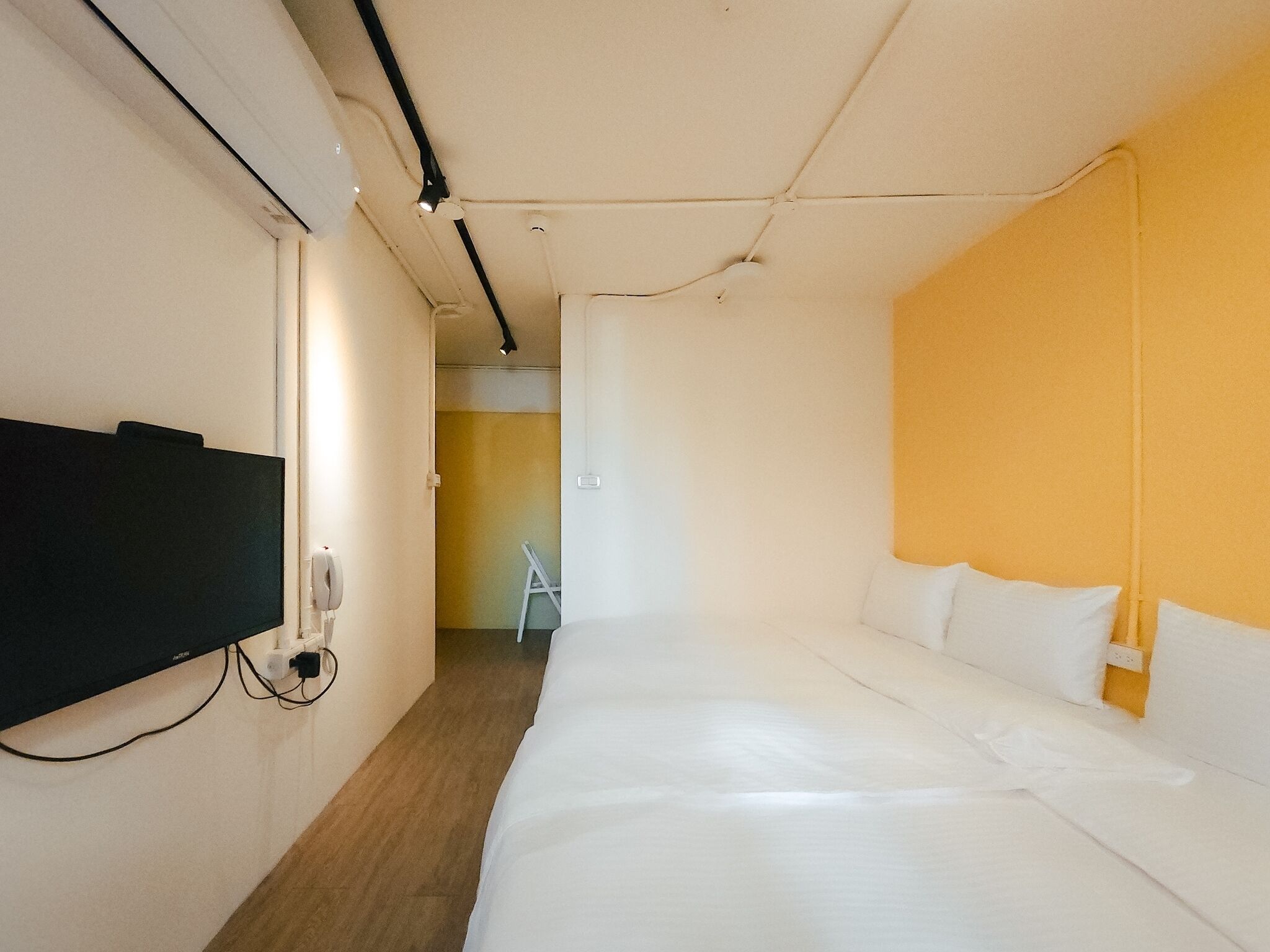 Quarto de hotel com uma cama, uma TV fixada na parede e uma escada ao fundo.