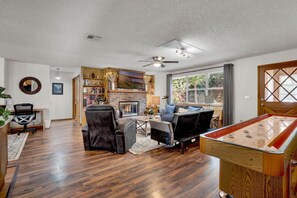 Uma sala de estar ampla com lareira, mesa de bilhar e uma grande janela com vista para o exterior.