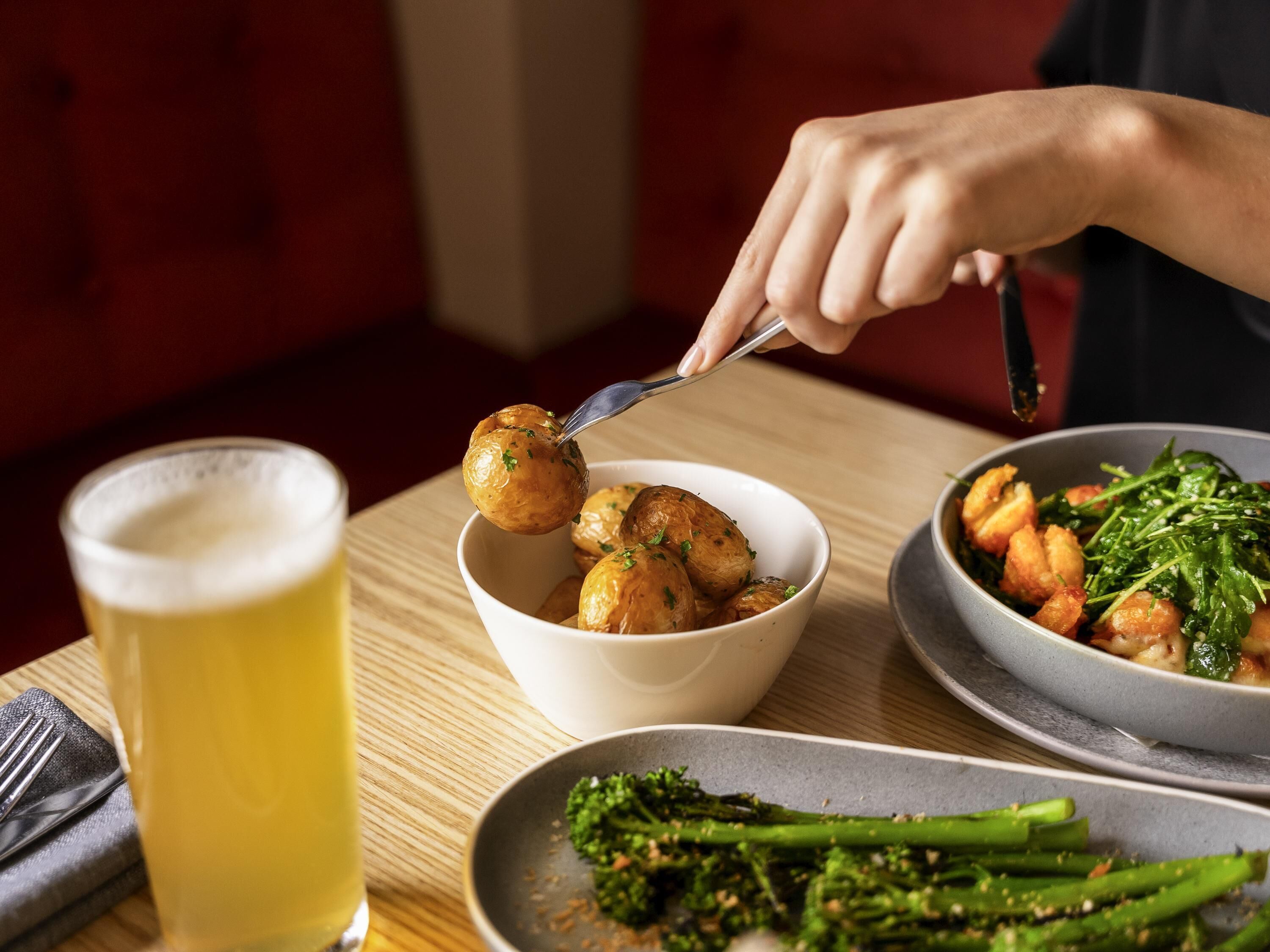 Uma mesa de jantar com uma tigela de comida, um copo de cerveja e um prato de brócolis.