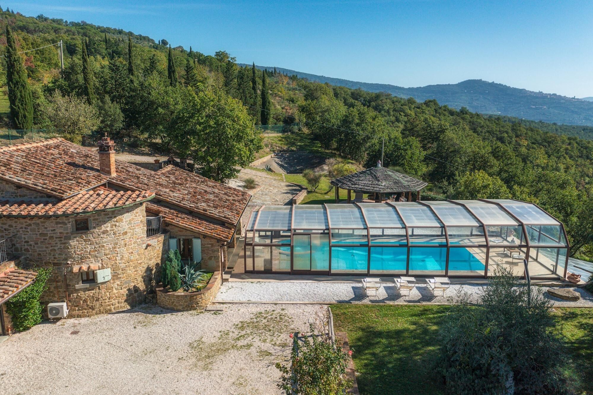 Uma casa com piscina, paredes de pedra e vista para a floresta ao redor.