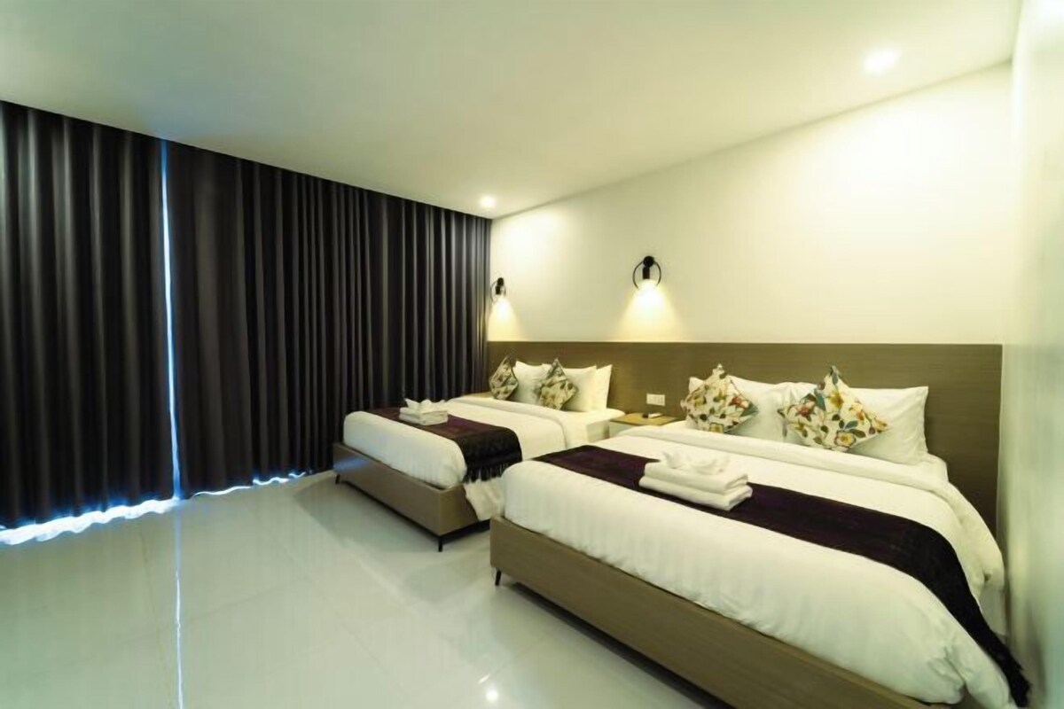 Quarto de hotel moderno com duas camas, cortinas escuras e iluminação embutida na parede.