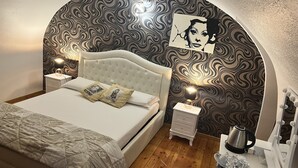 Quarto com cama grande, duas mesas de cabeceira com abajures, uma cafeteira e parede com padrão decorativo.