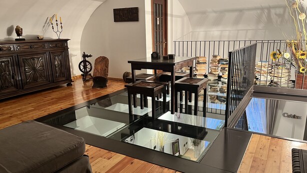Uma sala de estar moderna com uma mesa de centro de vidro, piso de madeira, um armário de madeira escura e uma escada que leva a um andar superior.