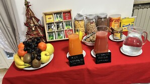 Uma mesa com toalha vermelha, um prato de frutas, jarra de suco e variedade de itens para o café da manhã.