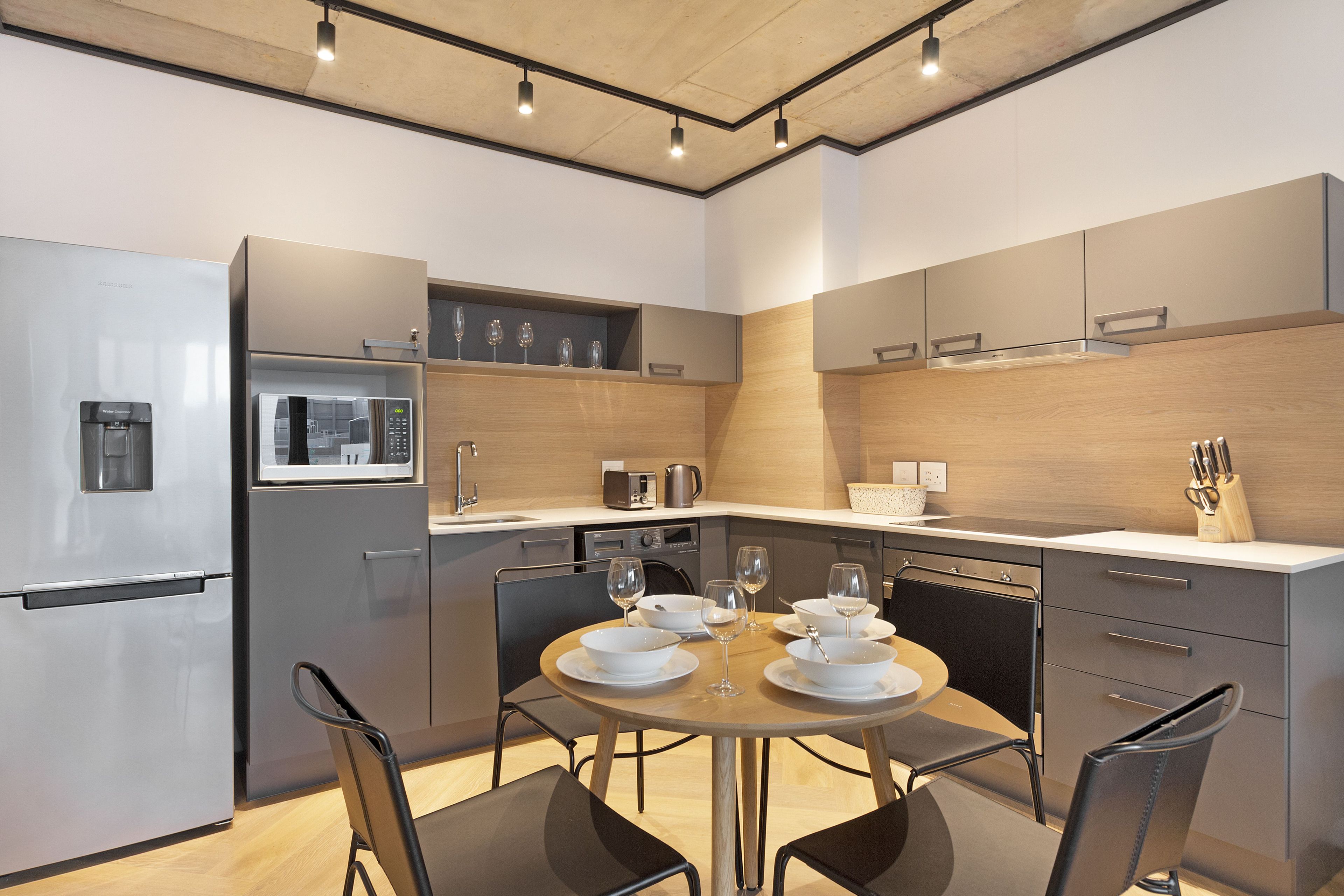 Uma cozinha moderna equipada com micro-ondas, forno e máquina de café. Há uma mesa de jantar com cadeiras e um conjunto de copos de vinho.