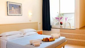 Quarto de hotel com cama, bandeja de café da manhã com frutas, um quadro na parede e vista para a varanda.