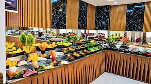 Buffet com diversos alimentos e uma mesa comprida com toalha marrom.