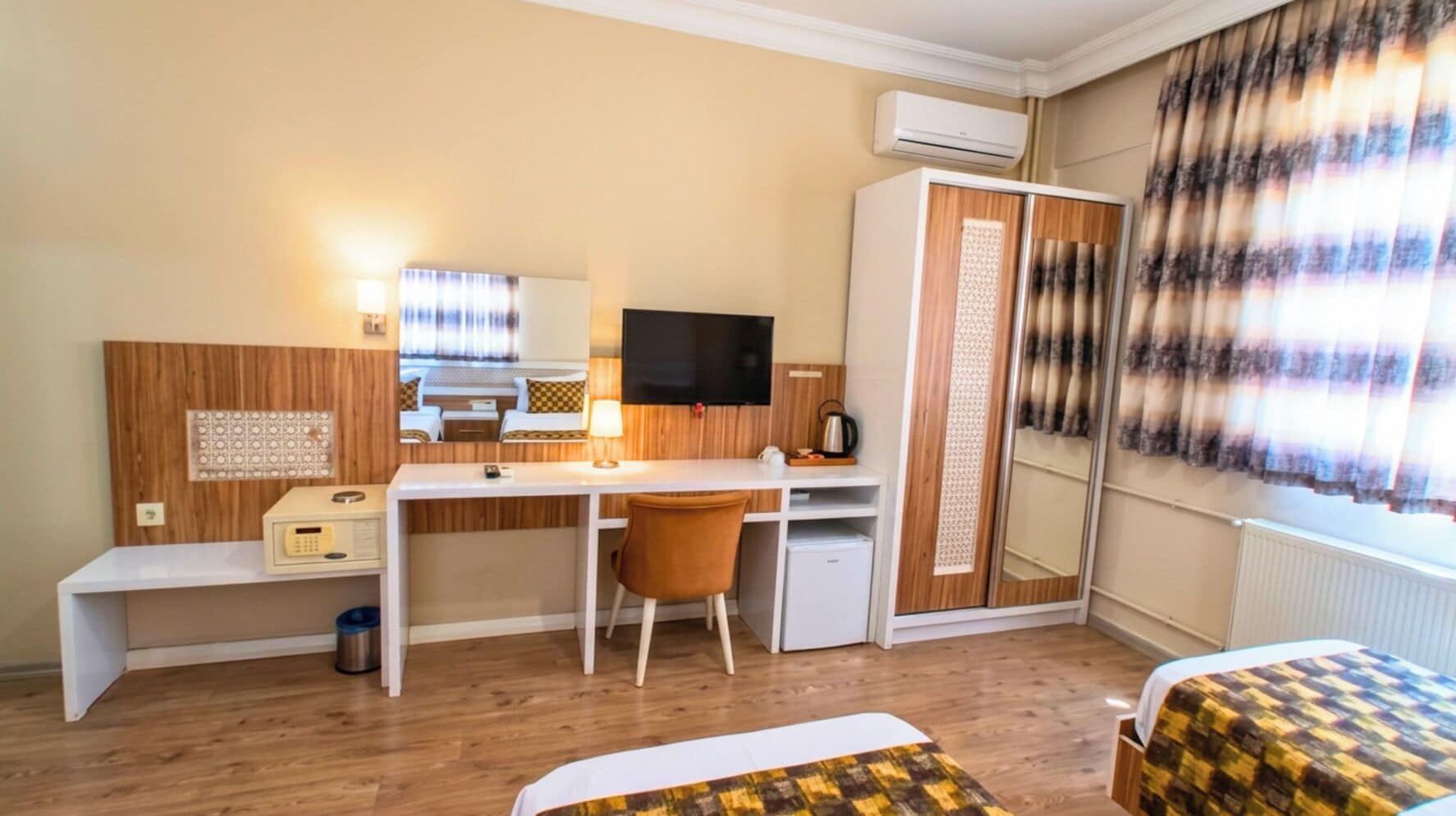 Quarto de hotel com escrivaninha, cadeira, cama, guarda-roupa e televisão.