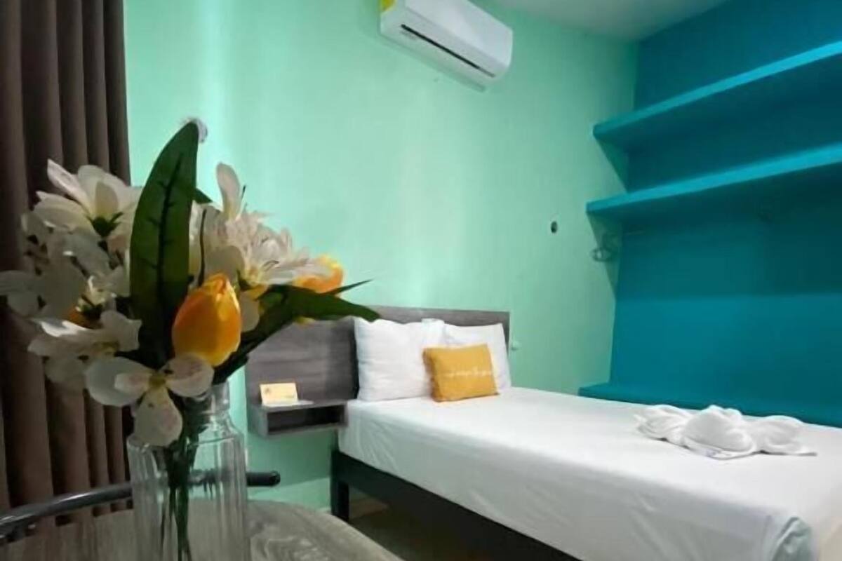 Quarto de hotel com uma cama, mesa de cabeceira, um vaso com flores e um ventilador de teto.