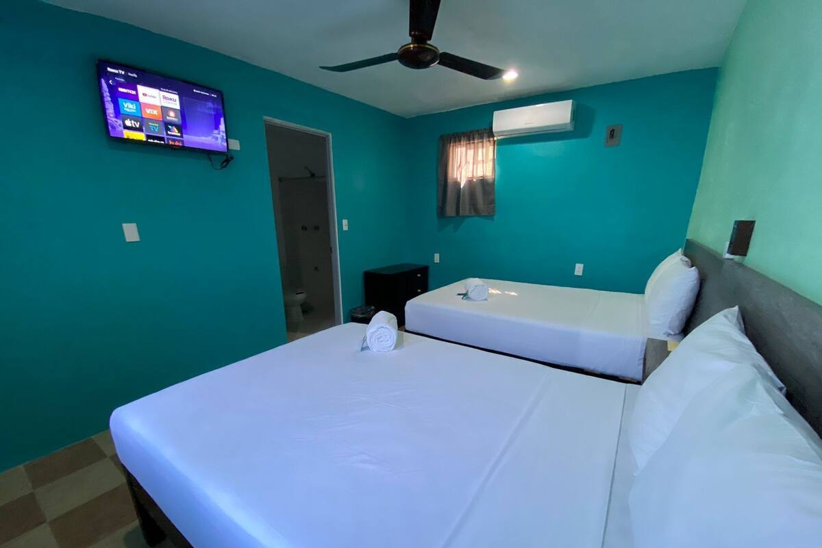 Quarto de hotel com uma cama grande, uma cama menor, uma TV fixada na parede e um ar condicionado.