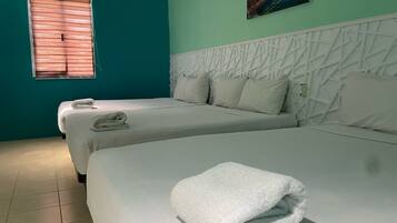 Quarto de hotel com duas camas, uma parede verde-água, um quadro de uma ponte e uma janela com persianas.