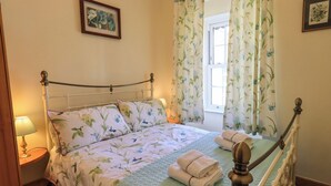 Cama bem arrumada com roupa de cama florida, luminária de cabeceira e vista para a janela do quarto.