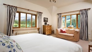 Quarto com uma cama grande, cômoda de madeira, sofá listrado e duas janelas com cortinas.
