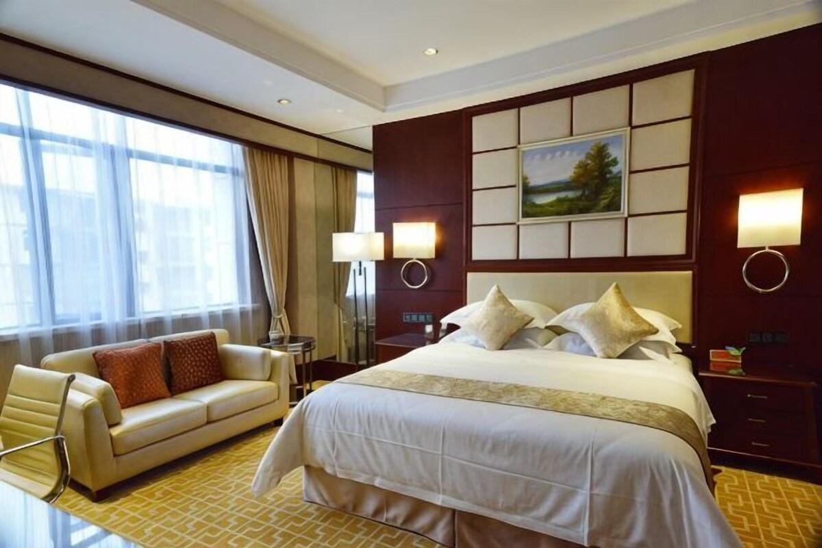 Quarto de hotel com uma cama grande, um sofá, uma escrivaninha e vista para a cidade.