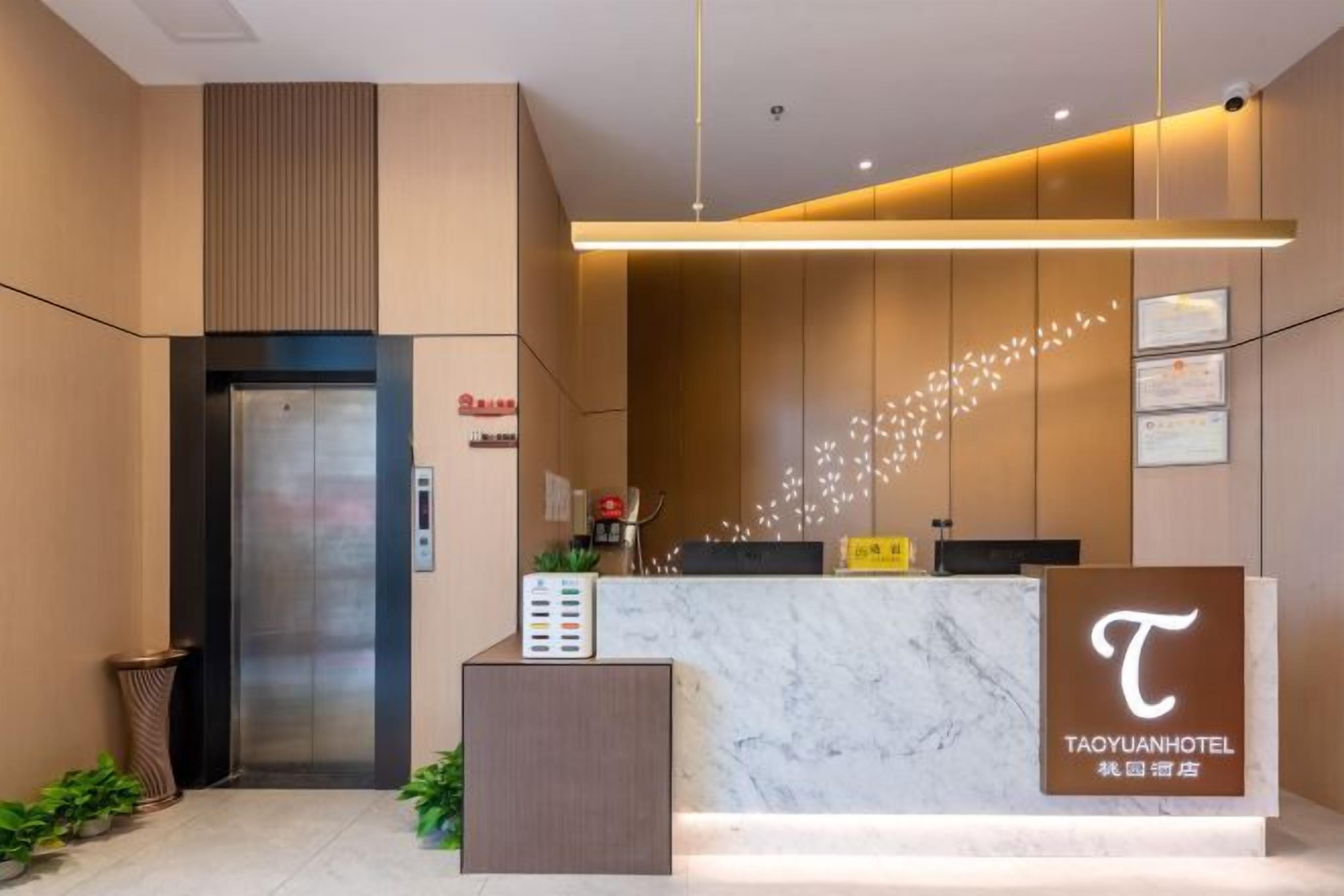 Uma área de recepção moderna de hotel, com balcão de mármore, mesa de atendimento e instalação luminosa vertical.