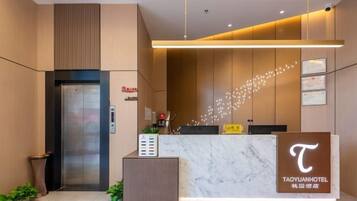 Uma área de recepção moderna de hotel, com balcão de mármore, mesa de atendimento e instalação luminosa vertical.
