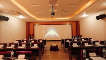 Uma sala de conferências com fileiras de mesas, uma tela de projetor e um projetor fixado no teto.