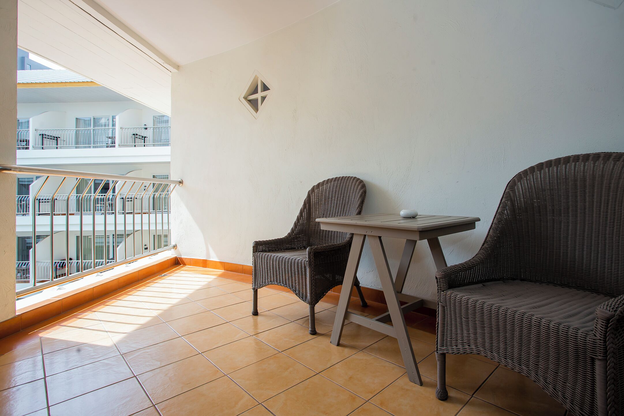 Uma varanda com móveis de vime, uma mesinha e vista para a fachada do edifício.