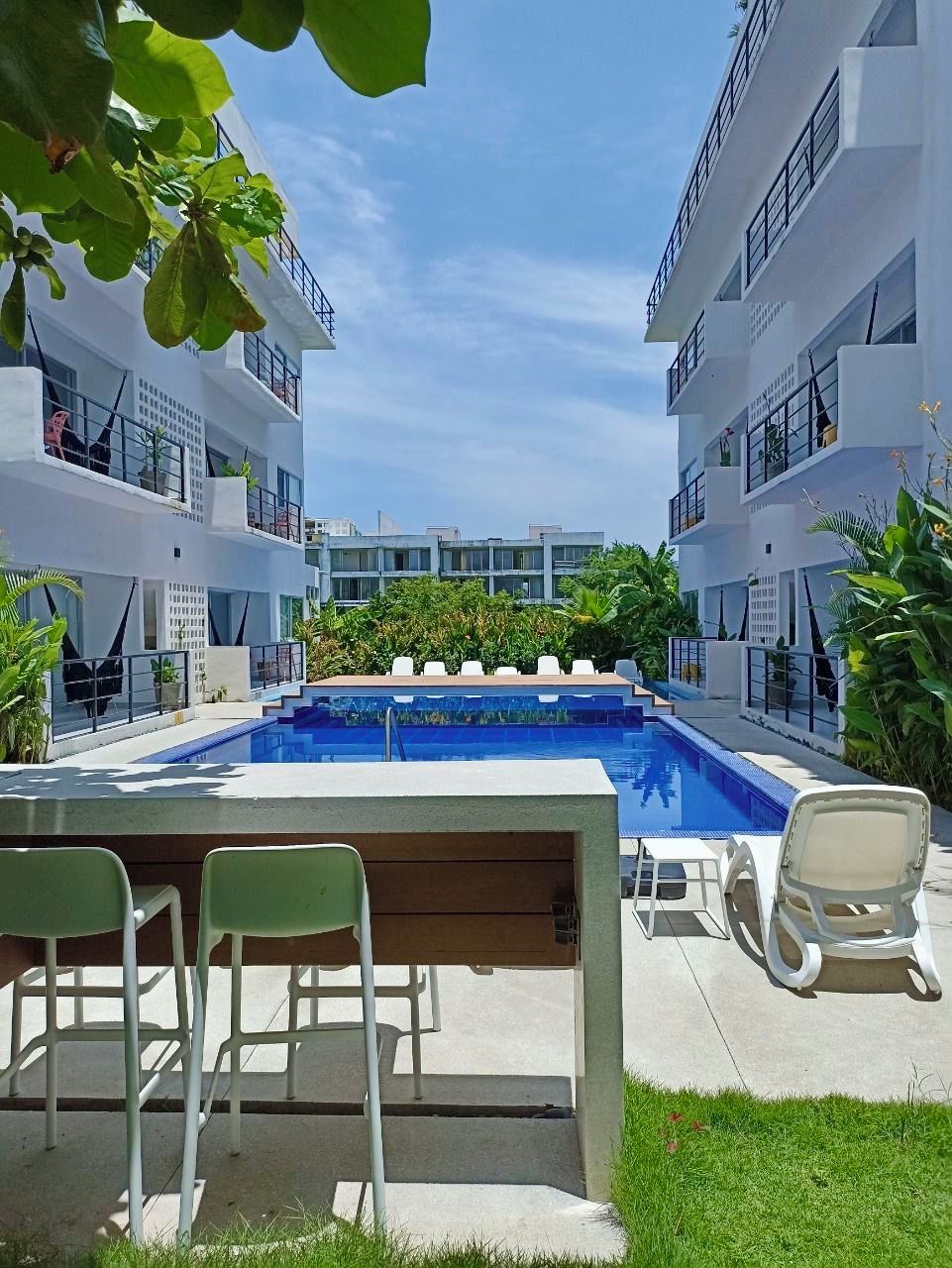 Uma área de piscina moderna, com uma piscina retangular, rodeada por edifícios brancos com varandas.