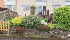 Um edifício residencial de dois andares com uma parede de pedra e diversas plantas em frente.