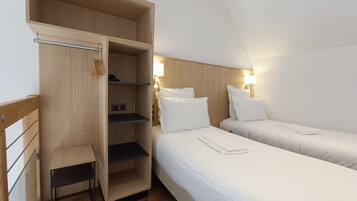 Quarto de hotel com duas camas, um guarda-roupa de madeira, uma mesa pequena e um banco.