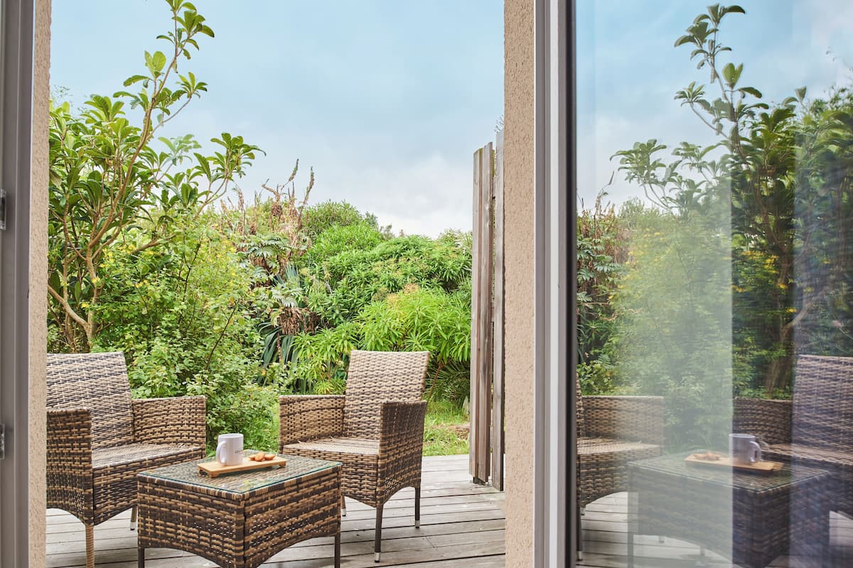 Um pátio externo com móveis de vime e uma porta de vidro que dá para um jardim exuberante.