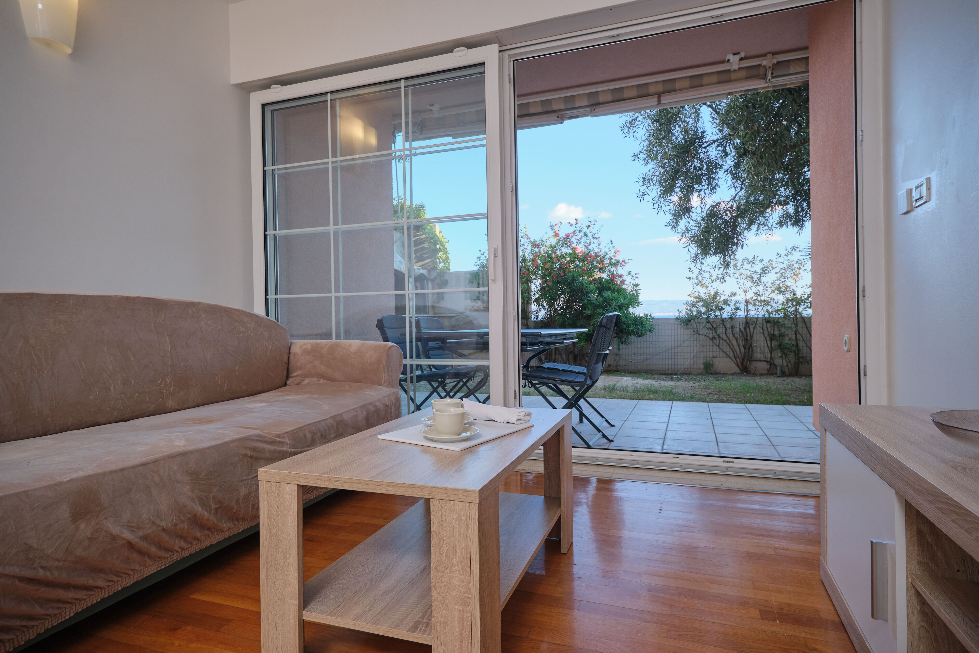 Uma sala de estar moderna com um sofá, uma mesa de madeira e uma porta de vidro deslizante que dá para um pátio externo.