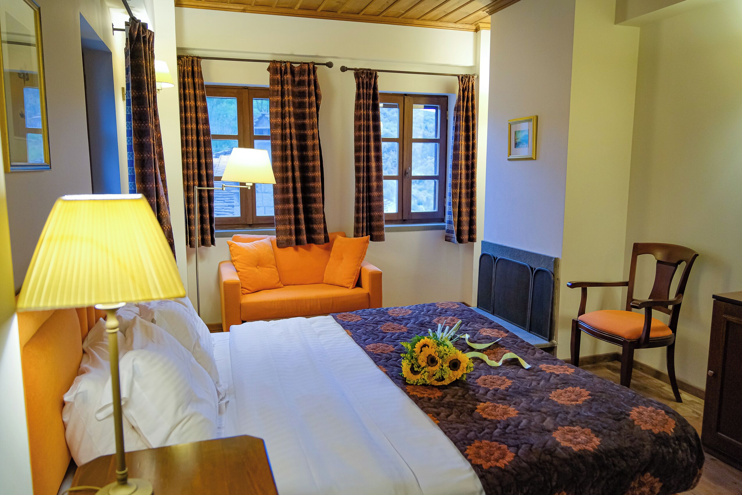 Quarto de hotel com cama, poltrona, luminária e janela com cortinas.