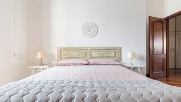 Quarto com cama, duas mesas de cabeceira, um prato decorativo fixado na parede e porta de madeira.