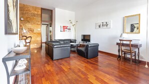 Uma sala de estar com sofá, mesa de centro, televisão e escrivaninha com cadeira.