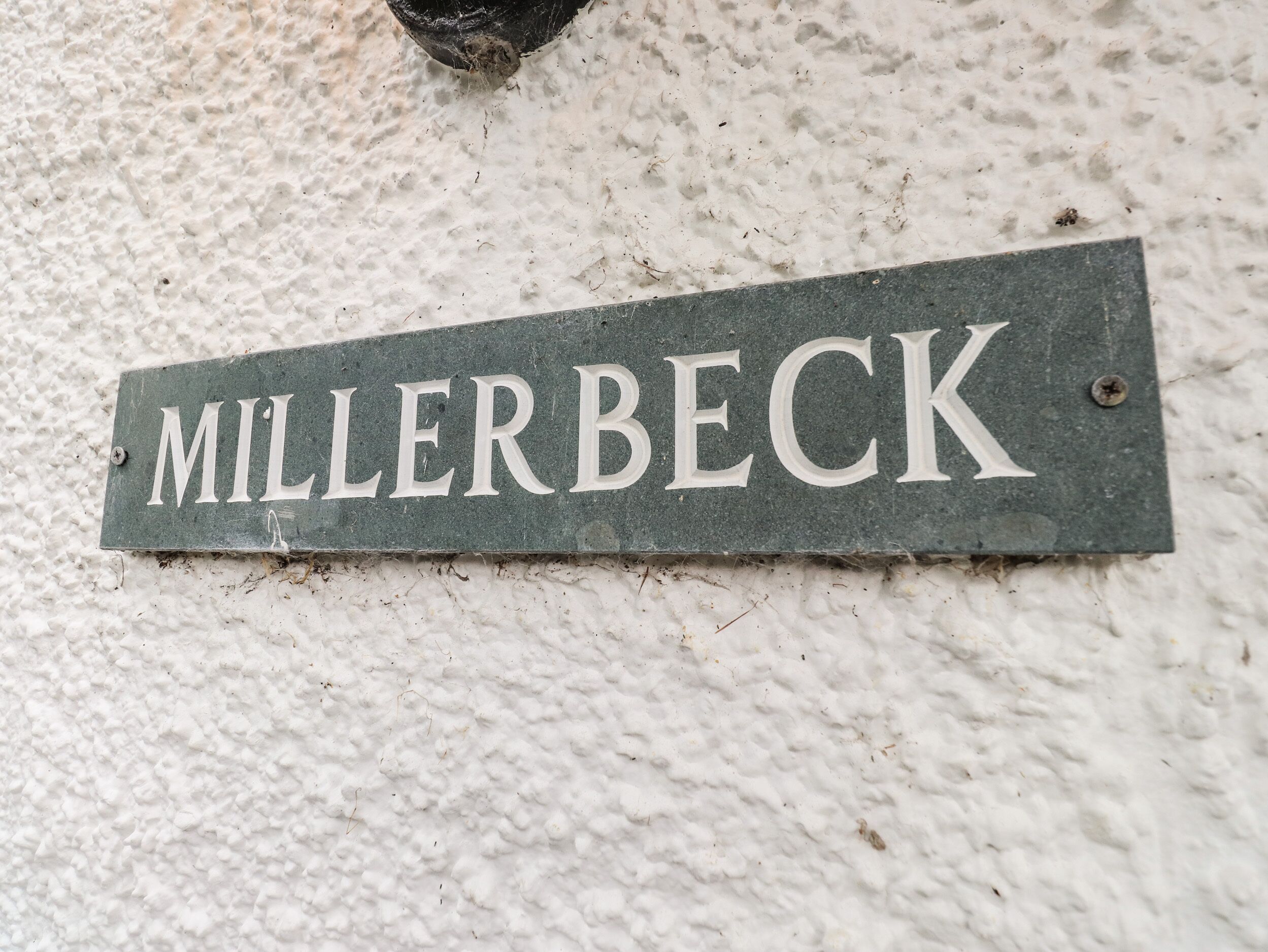 Placa com o nome 'MILLERBECK' fixada numa parede com textura.