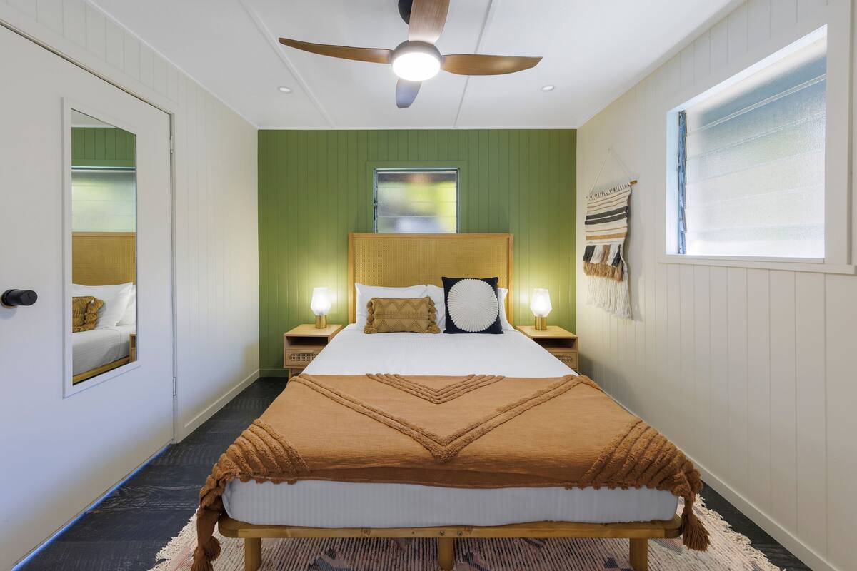 Quarto com cama, ventilador de teto, abajures, janela e espelho.
