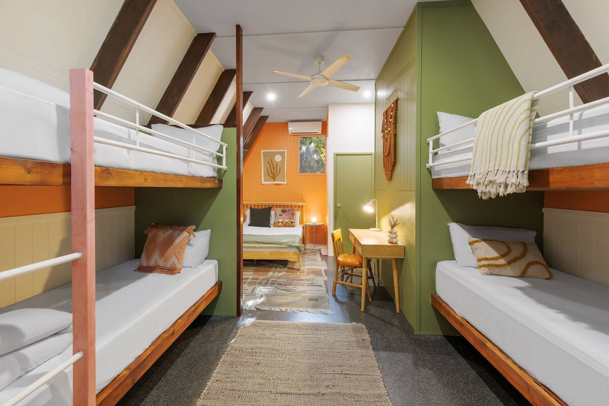 Quarto em dormitório com beliches, escrivaninha e ventoinha.