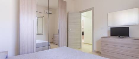 Um quarto com cama, cômoda, televisão e guarda-roupa.