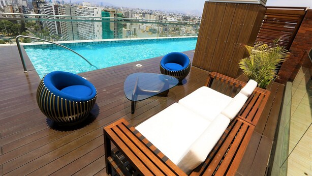Uma área de piscina no terraço com vista para a cidade, deck de madeira, espreguiçadeiras e mesa de vidro.