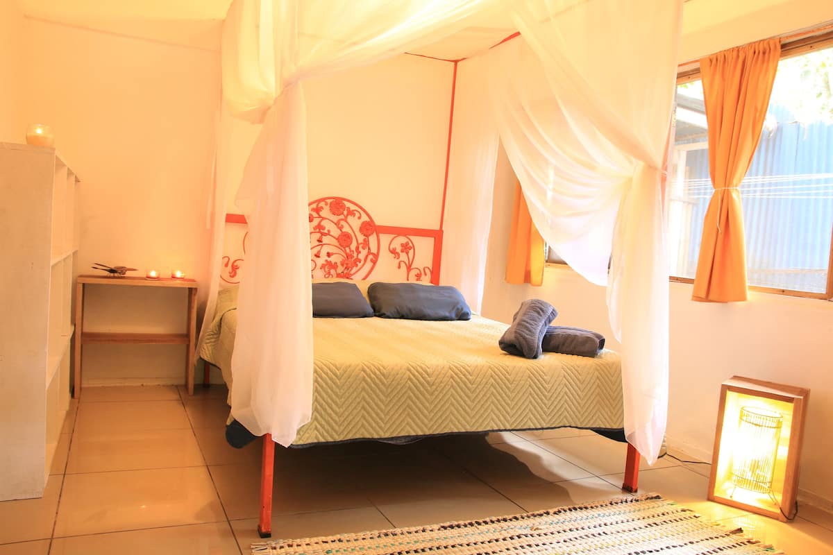 Um quarto com cama sob dossel, mesa de cabeceira com velas e criado-mudo.
