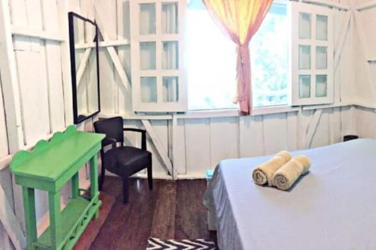 Um quarto com cama, escrivaninha, cadeira e janela com cortinas.