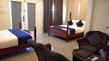 Quarto de hotel com duas camas, área de estar com móveis de vime e vista para o exterior.