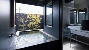 Uma casa de banho moderna com uma banheira de hidromassagem fechada em vidro, um espelho grande e vista para uma árvore lá fora.