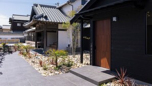 Uma casa japonesa tradicional com uma extensão moderna, apresentando um caminho de pedra e pequenas plantas.