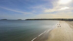 Uma praia com águas cristalinas, areal dourado e colinas ao longe.