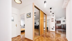 Um corredor com piso de madeira, uma porta deslizante e uma cozinha ao fundo.