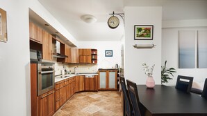 Cozinha moderna com armários de madeira, mesa de jantar, cadeiras e um relógio na parede.