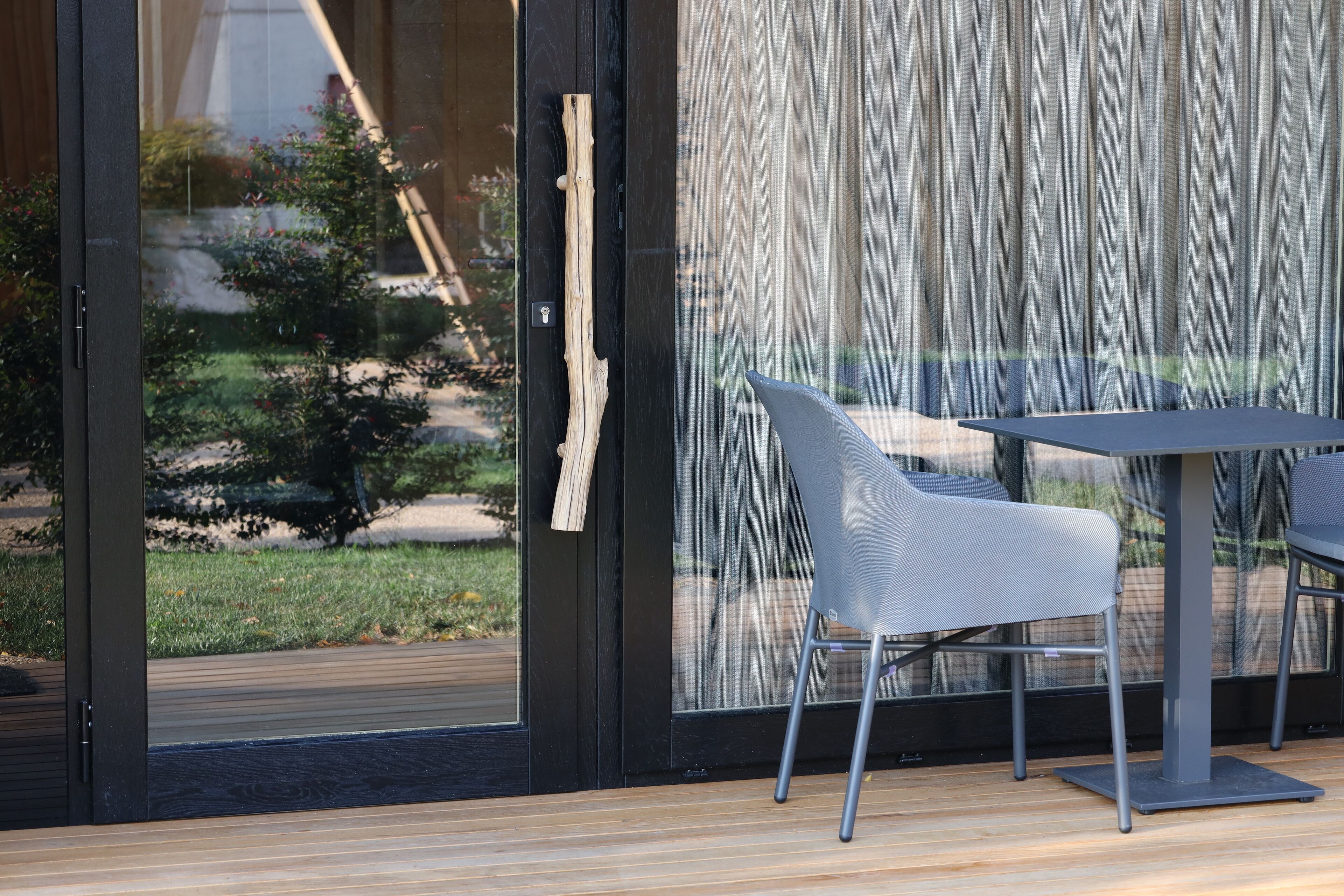 Uma área externa moderna com espaço para sentar, uma mesa e duas cadeiras, um deck de madeira e uma porta de vidro que dá para um jardim.