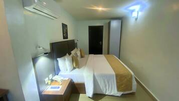Quarto de hotel com cama, mesa de cabeceira, abajur e ar condicionado.