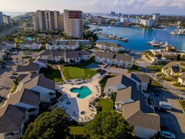 Zona residencial com piscina central rodeada por casas, marina com barcos e uma praia ao fundo.